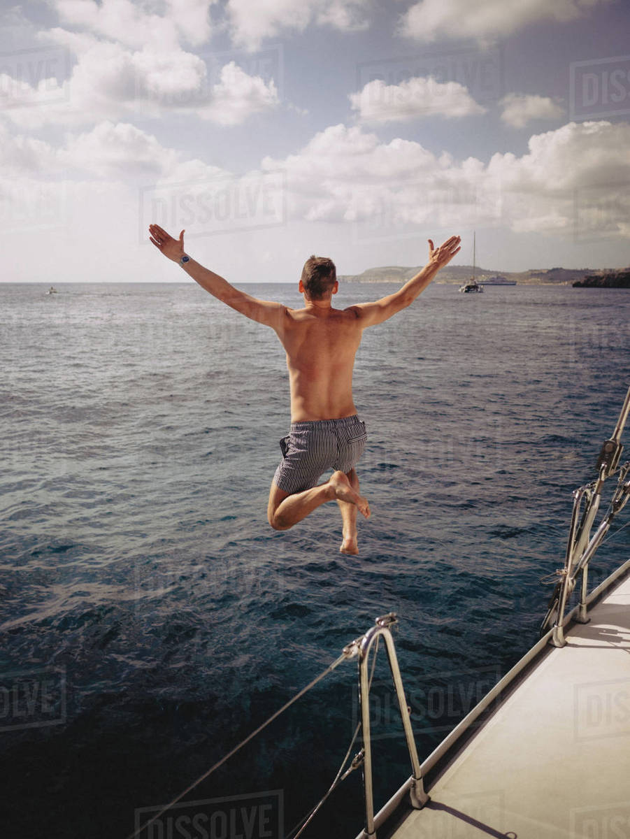 Full length rear view of man jumping from boat into sea on sunny day ...
