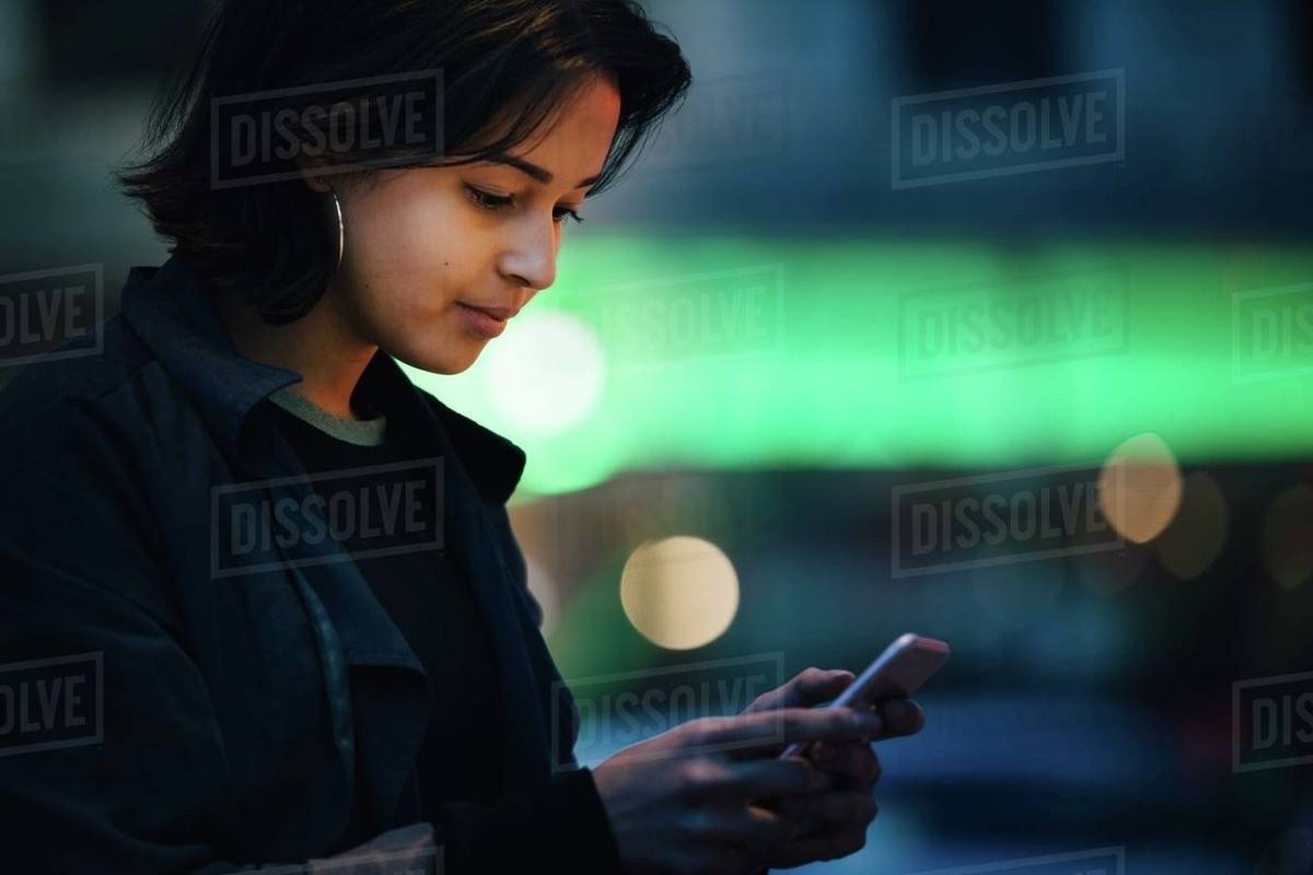 Young woman texting through mobile phone while standing in city at ...