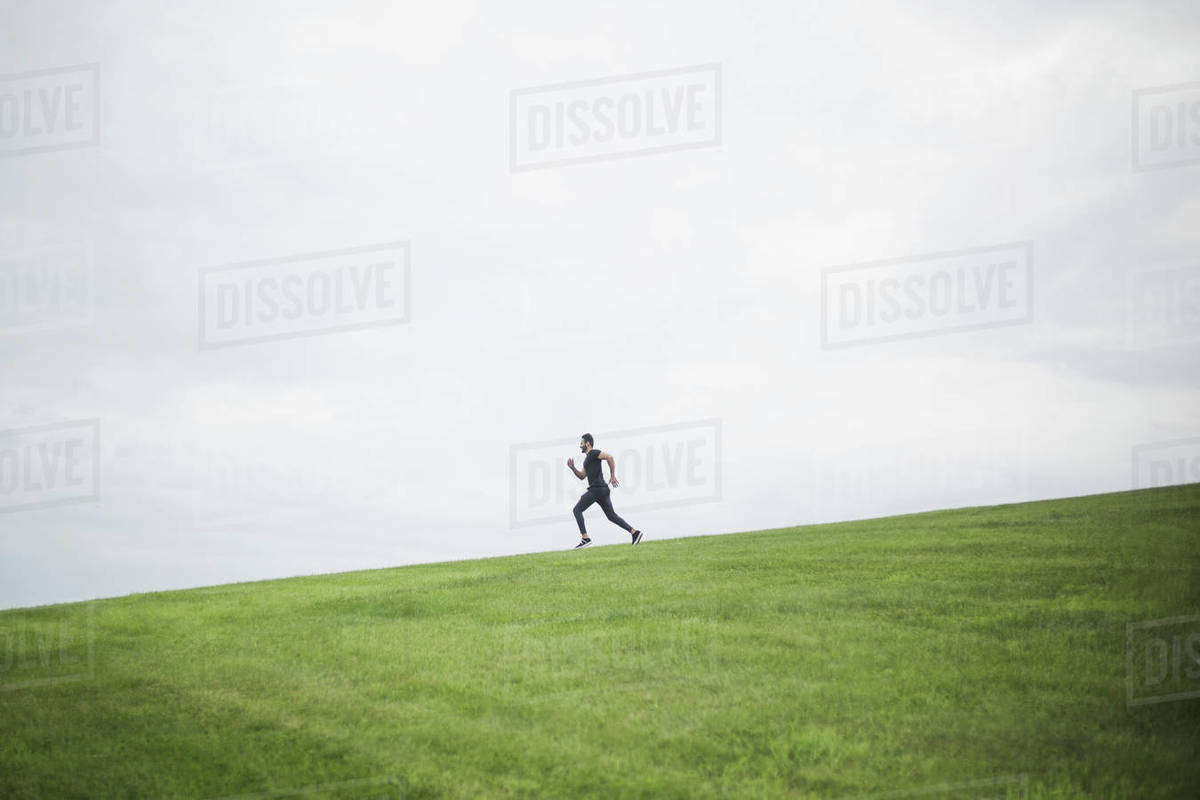 Side view of young man running on field against cloudy sky - Royalty ...