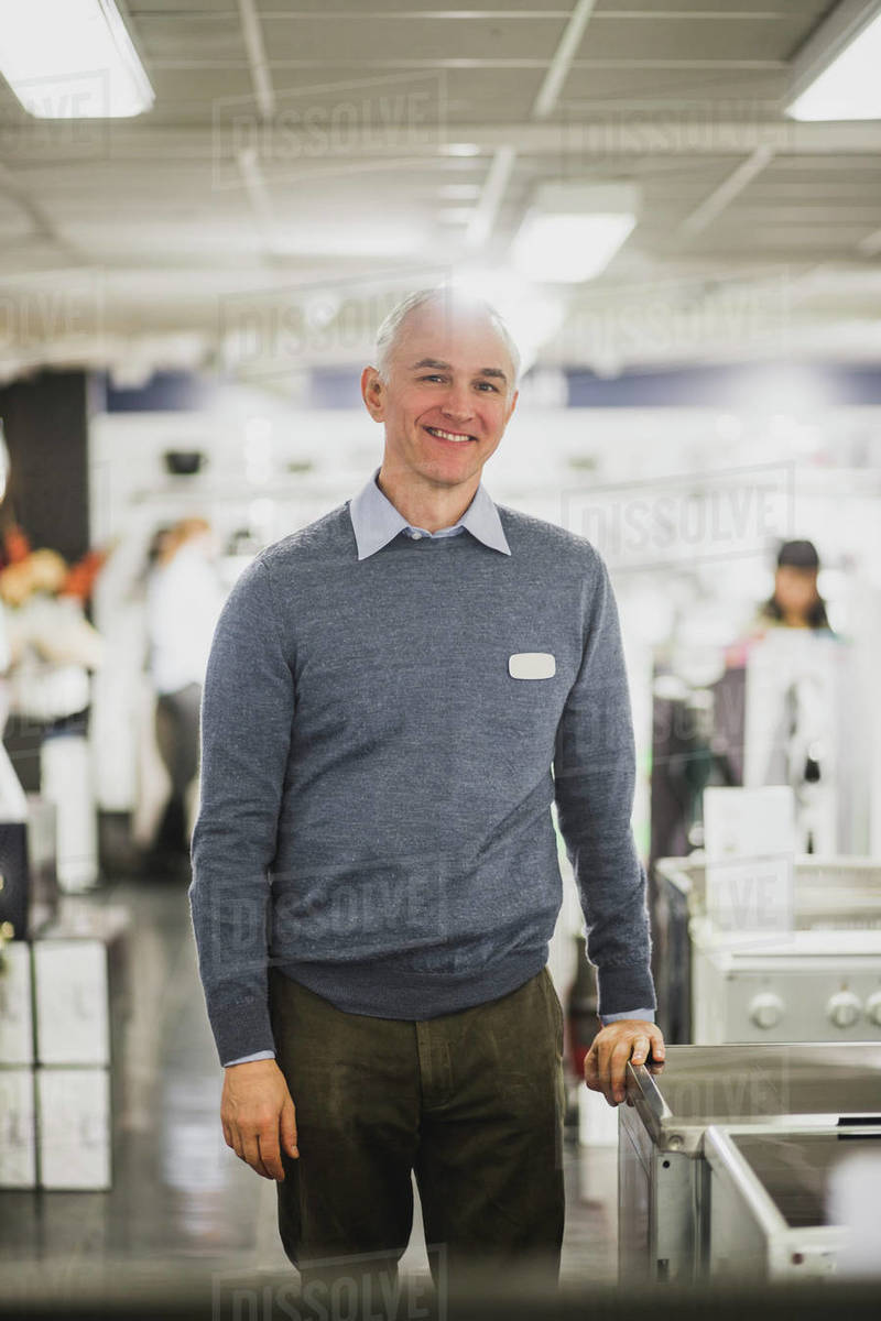 Portrait of smiling mature salesman standing in electronics store ...