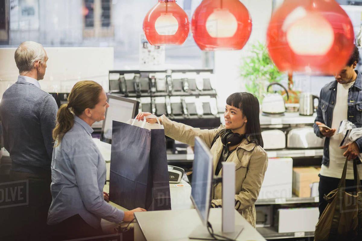 Smiling customer holding shopping bag while talking mature owner in ...