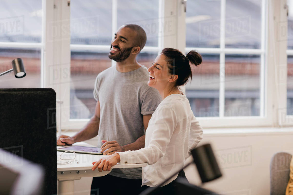 Happy professionals looking away while standing at office desk ...
