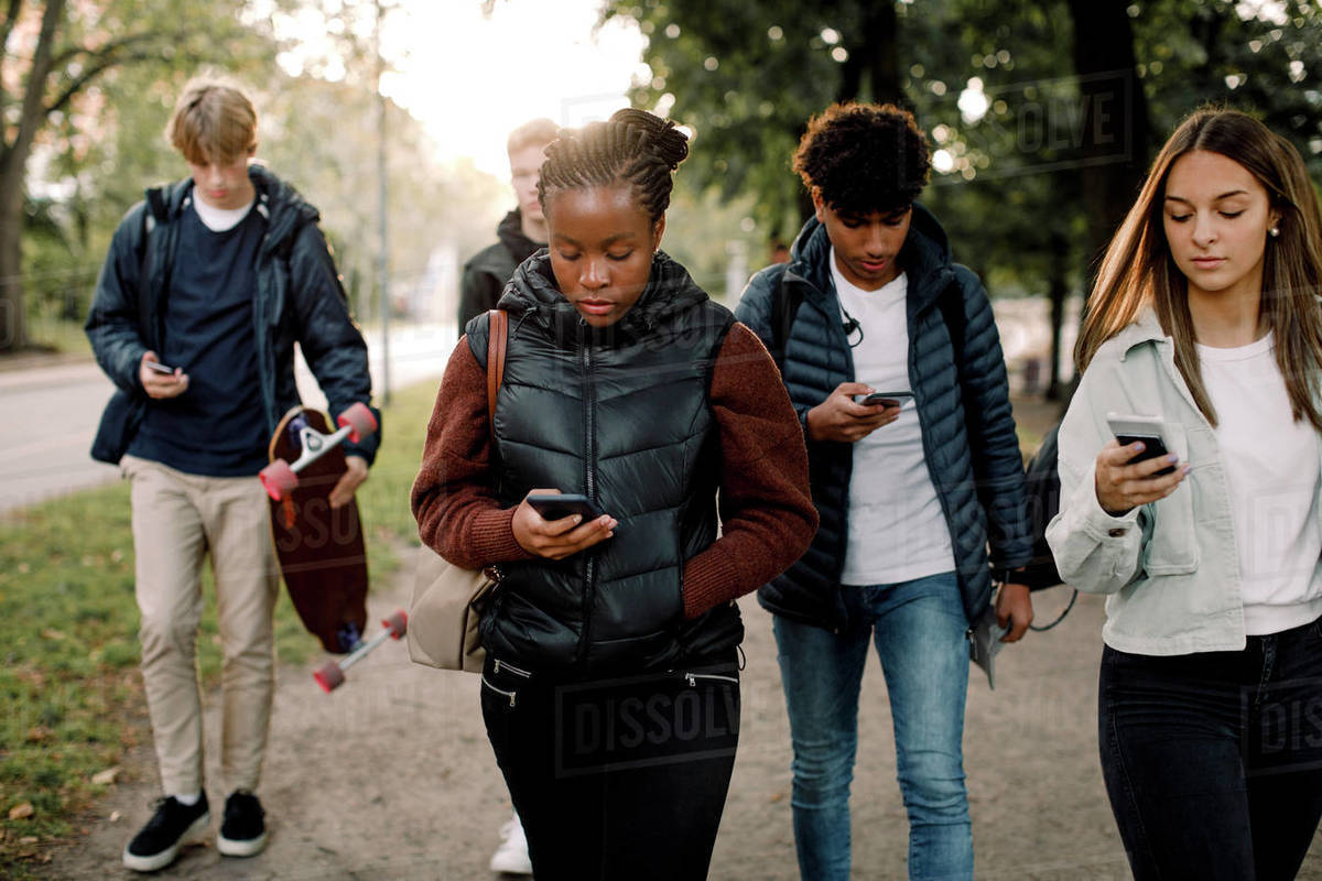 Multi-ethnic teenage friends using smart phones while walking on street in city - Stock Photo ...