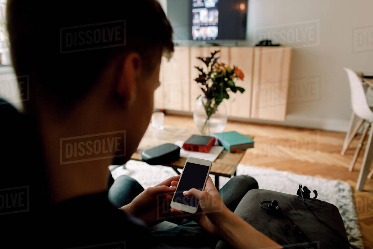 Teenage boy using smart phone while sitting on sofa at home - Royalty ...