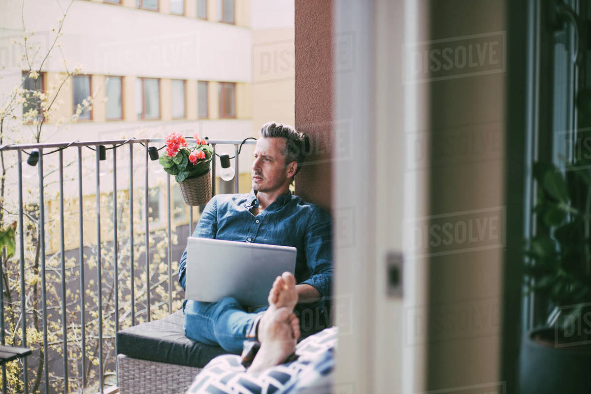 Man sitting on balcony with laptop looking out - Royalty-free Stock ...