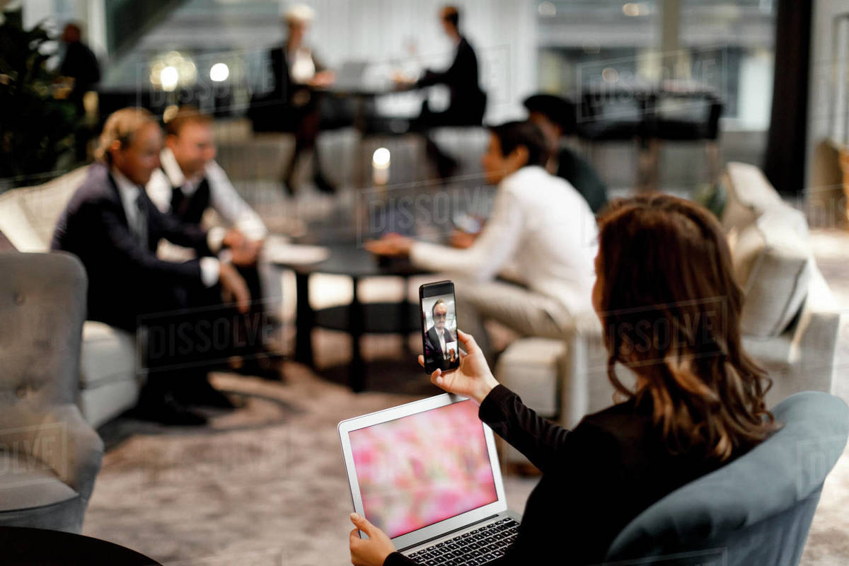 Businesswoman talking through video call while colleagues discussing in ...
