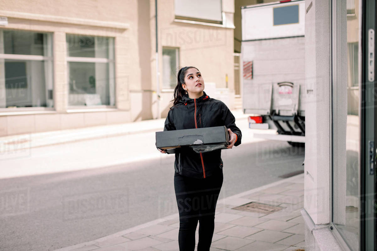 Young delivery woman delivering package at building - Stock Photo ...