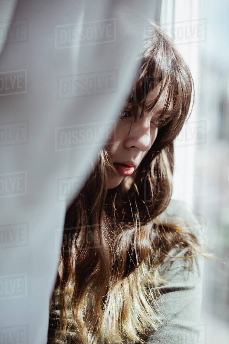 Close-up of young woman hiding behind window curtain - Stock Photo ...