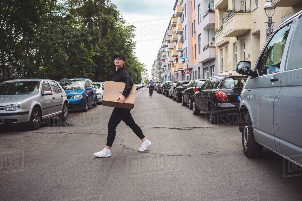 Side view of delivery woman with cardboard box walking on street in ...