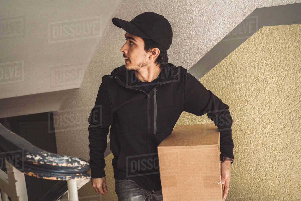 Delivery man with package looking away while walking on staircase ...