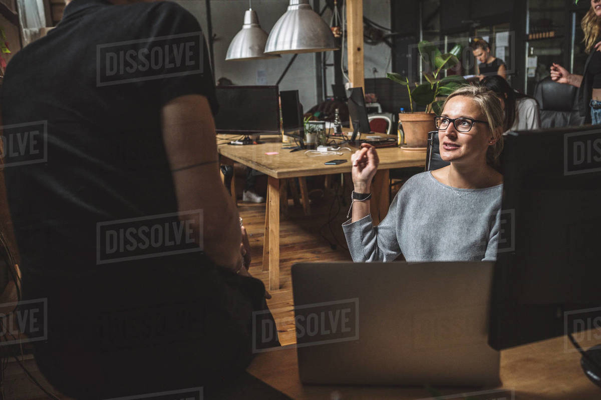 Smiling female computer programmer talking to coworker at workplace ...