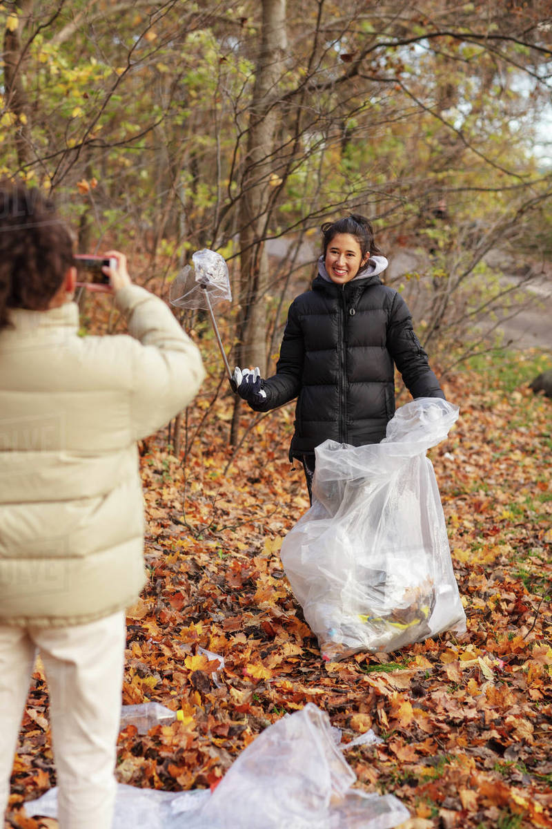 Young female environmentalist photographing smiling teenager holding ...