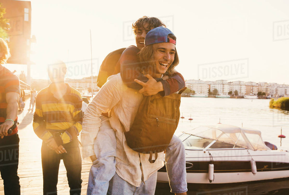 Cheerful teenager giving piggyback ride to friend at harbor - Stock ...