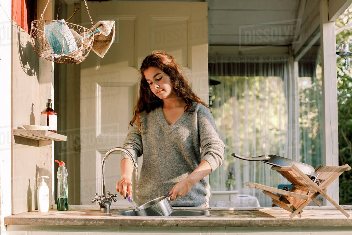 Teenage girl washing utensil in sink outside house - Royalty-free Stock ...