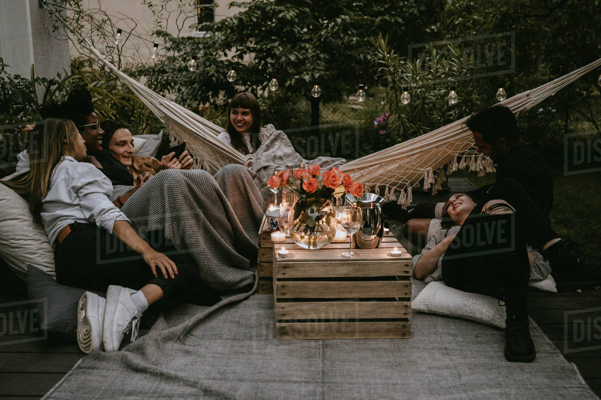 Smiling friends enjoying at social gathering in yard during sunset ...