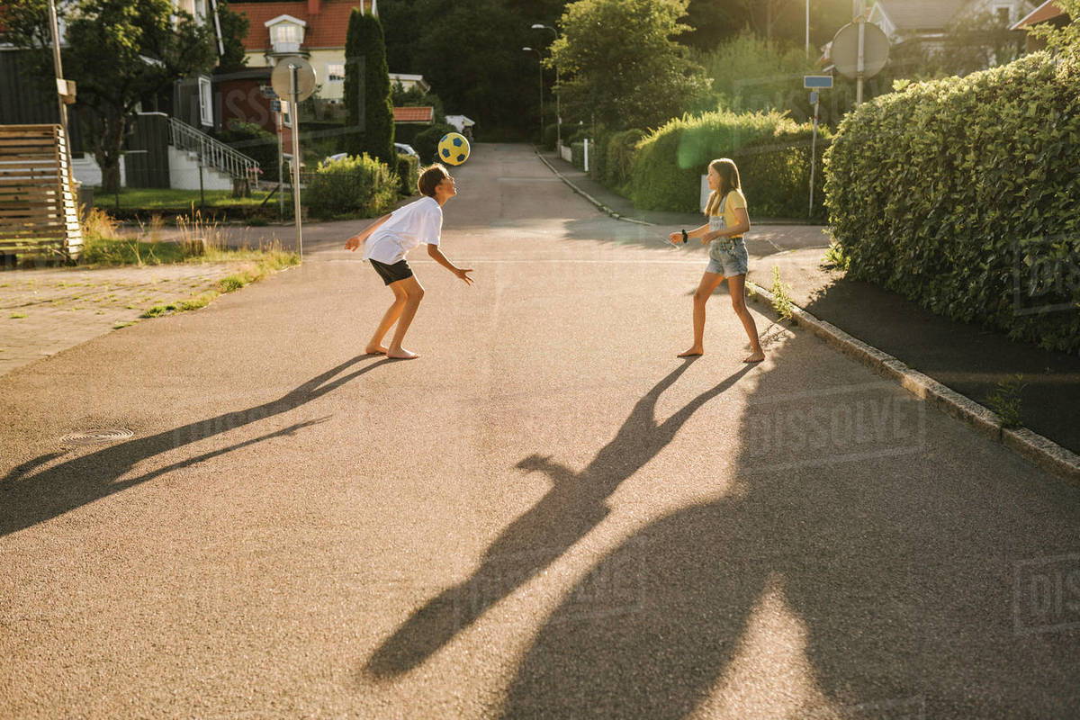 Siblings playing with soccer ball on road during sunny day - Royalty ...