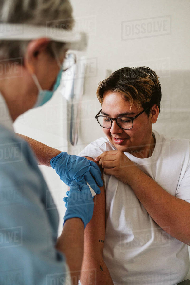 Senior female medical expert injecting male patient during COVID-19 ...