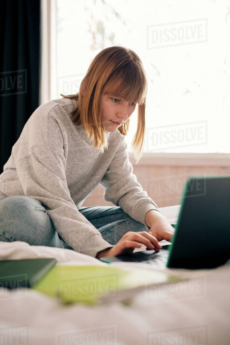 Teenage girl typing on laptop while doing homework at home - Royalty ...