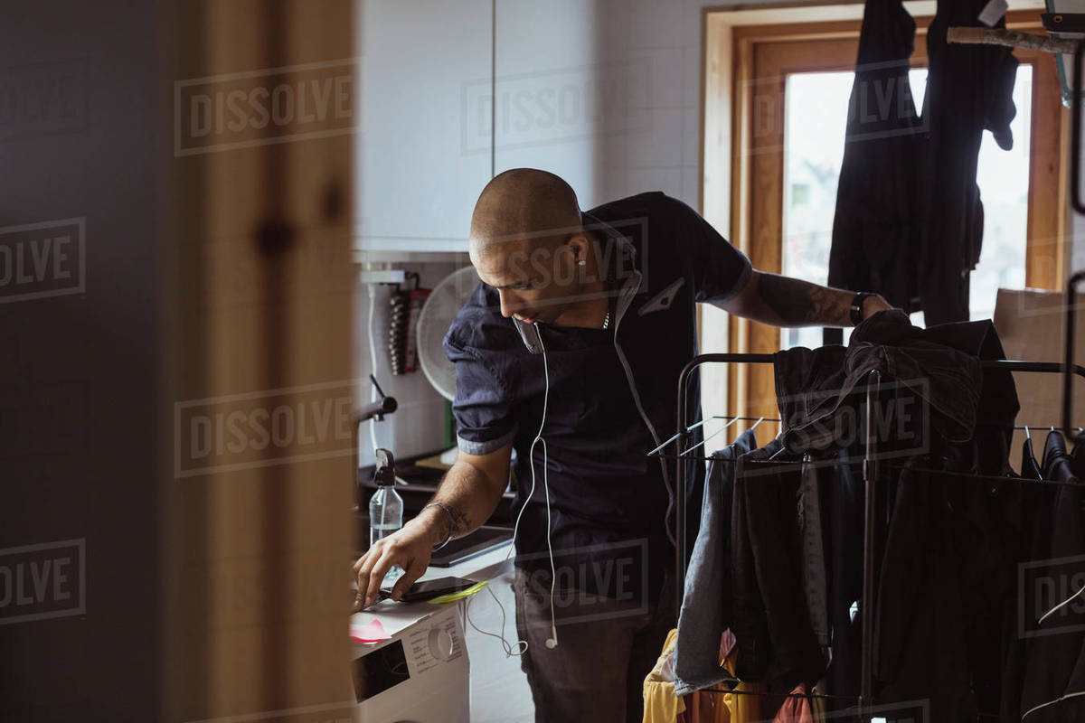 Bald man looking at washing machine while doing laundry chores in ...