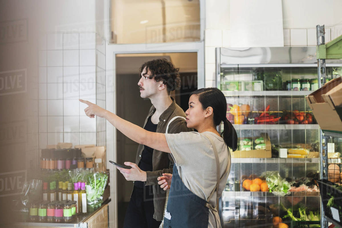 Female employee pointing while discussing with male customer in store ...