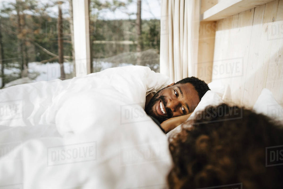 Smiling man lying with girlfriend on bed in cottage - Royalty-free ...