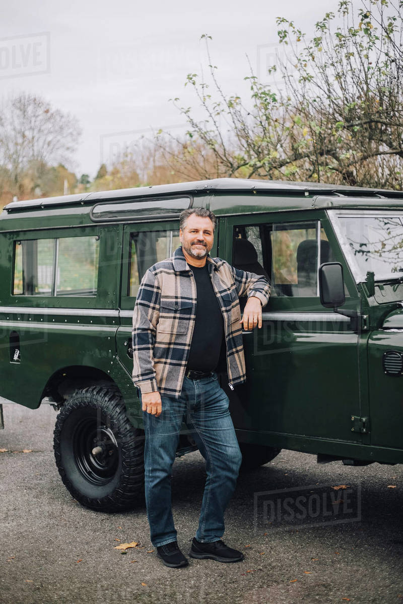 Portrait of mature man standing by sports utility vehicle on driveway ...