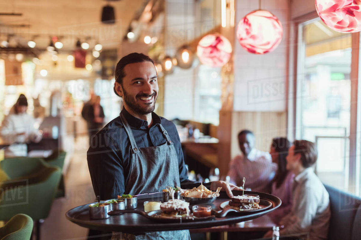 Portrait of smiling waiter with food while customer sitting in ...