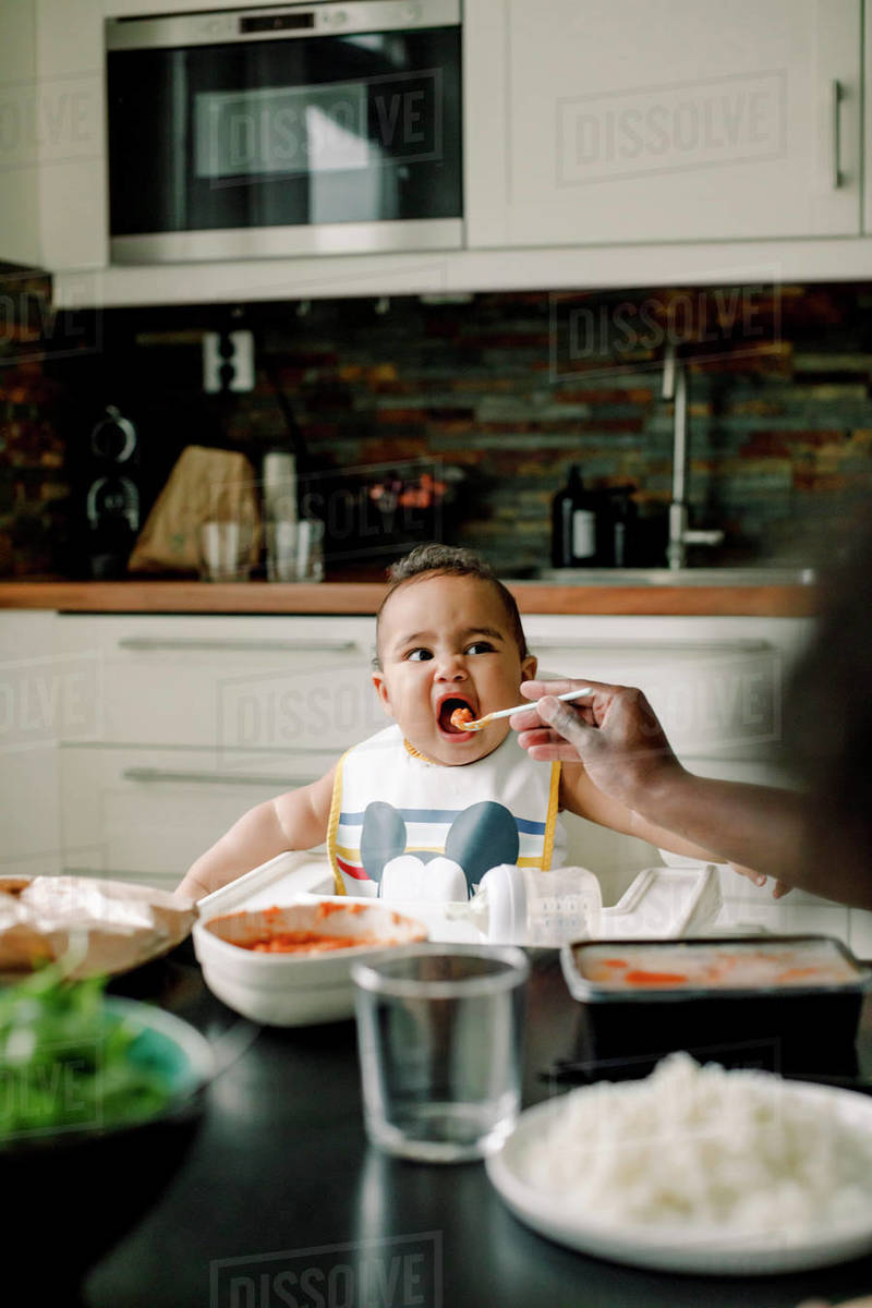 Cropped image of father feeding baby boy at dining table in kitchen ...