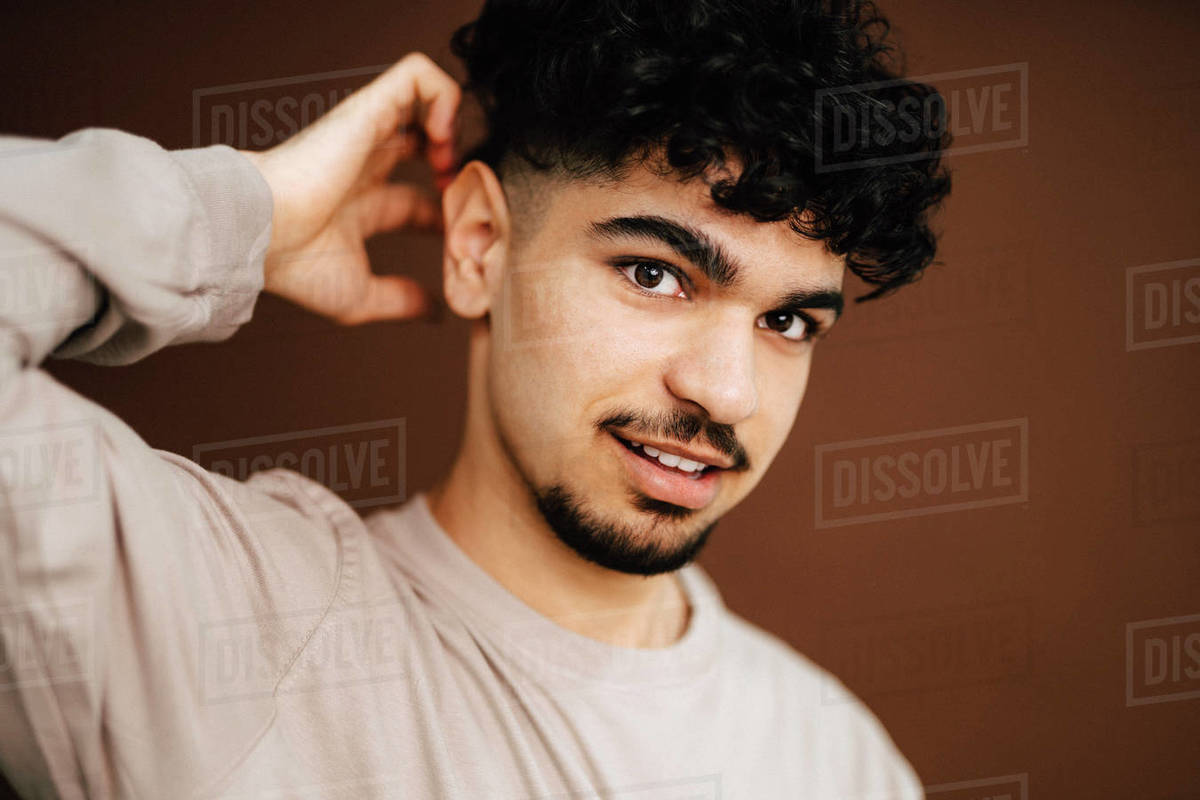 Young man with hand behind head in studio - Stock Photo - Dissolve