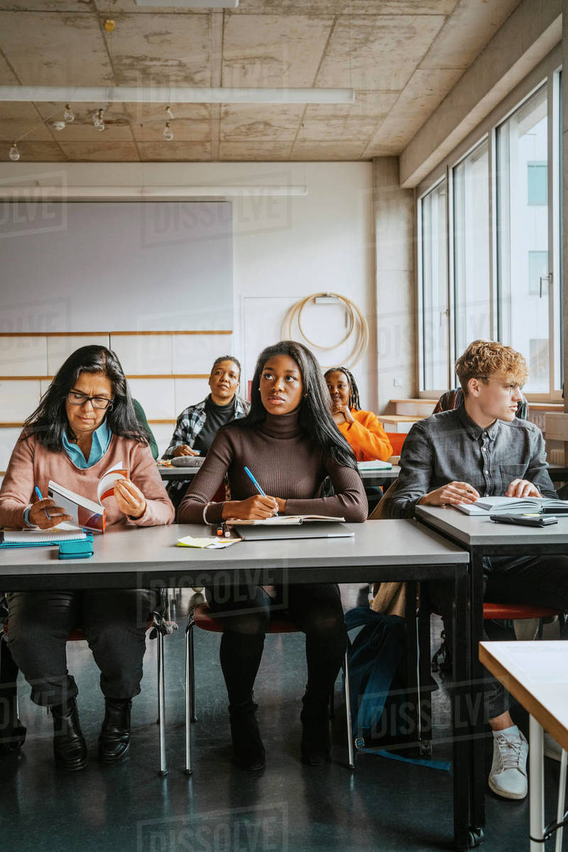 Multiracial university students sitting at desk learning in classroom ...