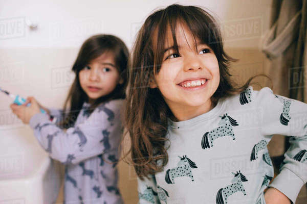 Happy girl standing with sister holding toothbrush in bathroom ...