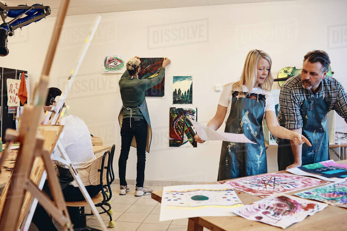 Male and female artists discussing over paintings while painter ...