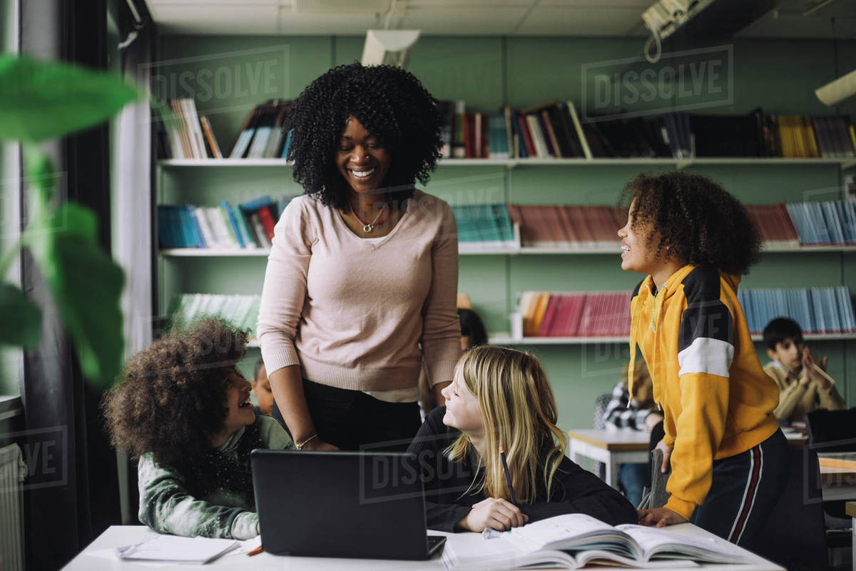 Smiling teacher interacting with students while doing e-learning in ...