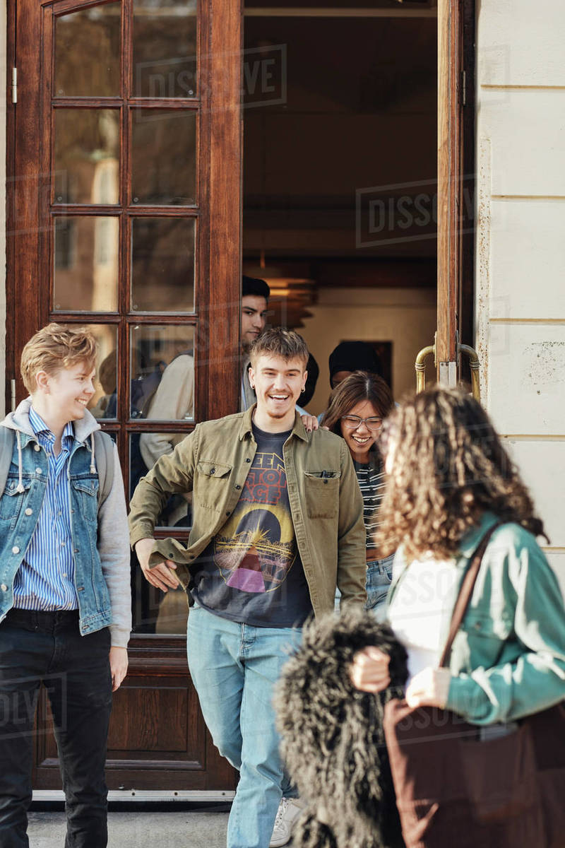 Happy male and female students walking out through university door ...