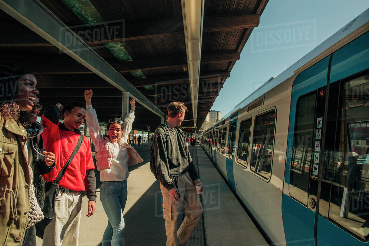 Happy multiracial friends cheering up on arrival of train at railroad ...
