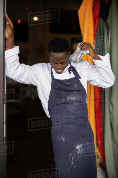 Happy chef looking down while standing at entrance of restaurant ...