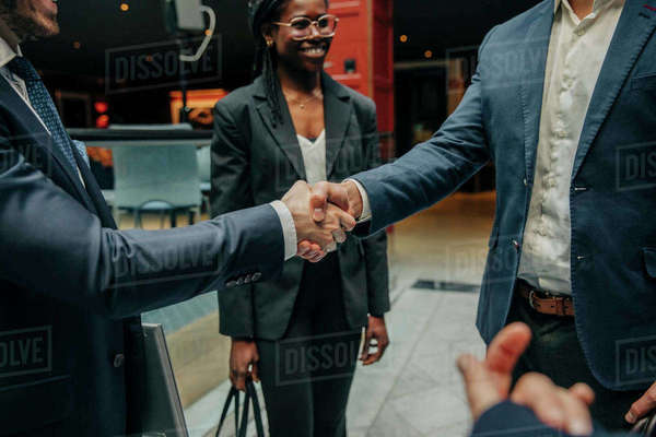 Businessmen handshaking by female colleague in hotel lounge - Royalty ...