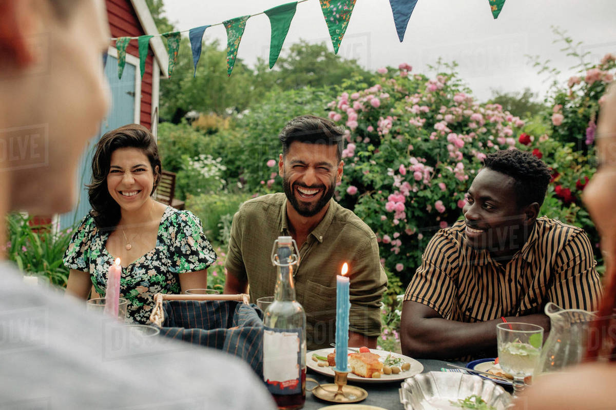 Man laughing while sitting at table with male and female friends during ...