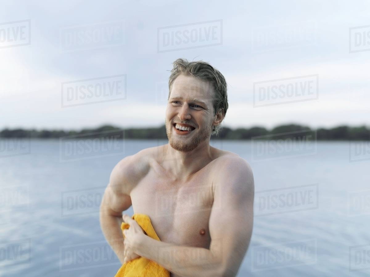 Bare chested young man drying off with towel, looking away smiling ...