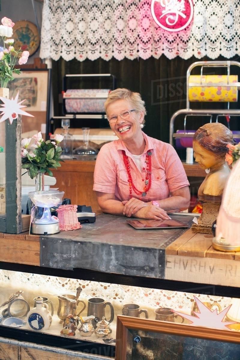 Portrait of happy mature woman behind vintage shop counter - Royalty ...
