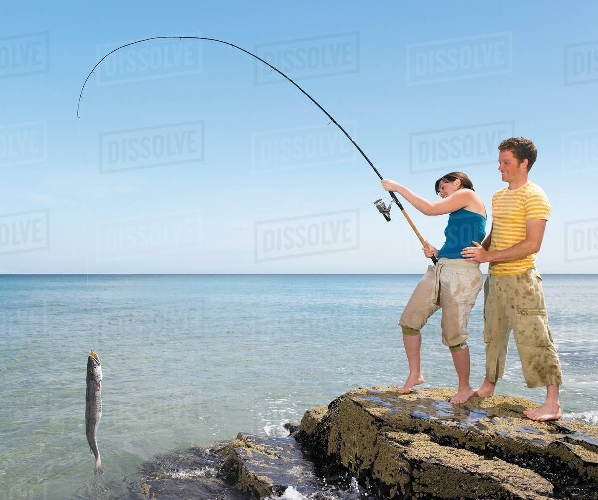 Couple landing a big fish off rocks - Royalty-free Stock Photo | Dissolve