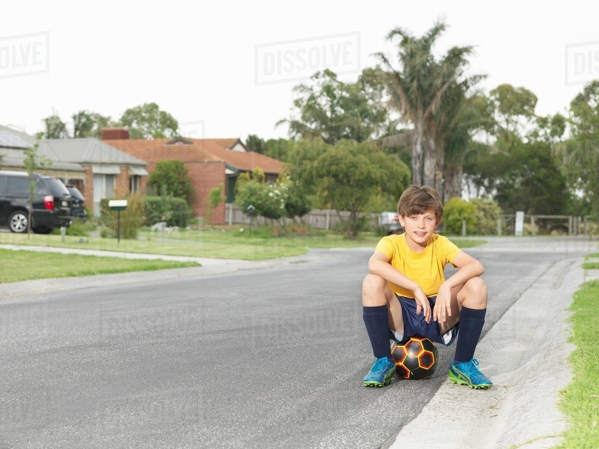 Portrait of boy sitting on soccer ball on suburban road - Stock Photo ...