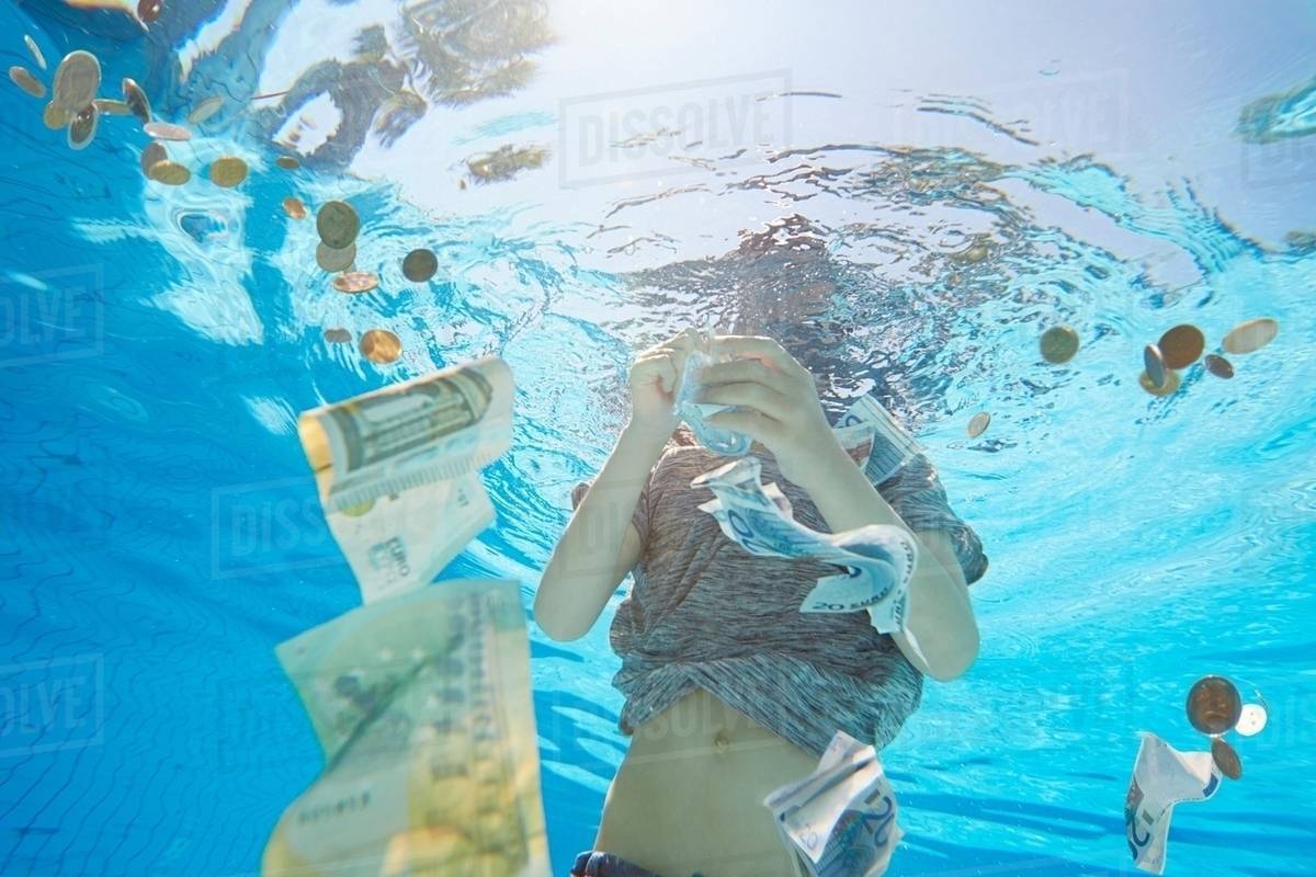 Underwater view of boy in swimming pool grabbing euro currency ...