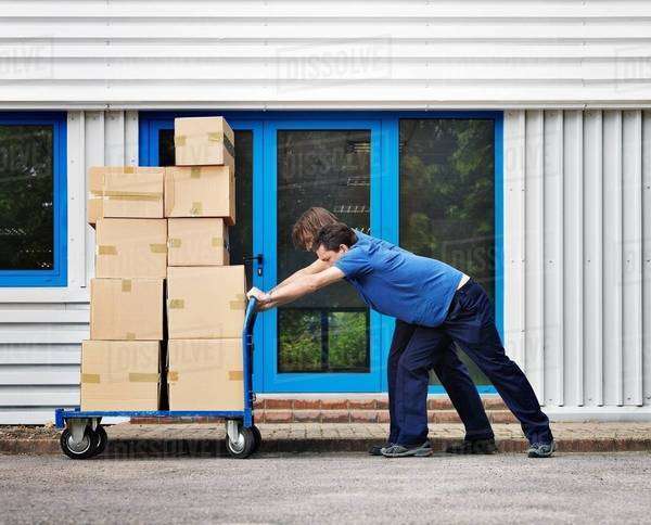 Two men moving boxes on trolley - Royalty-free Stock Photo | Dissolve