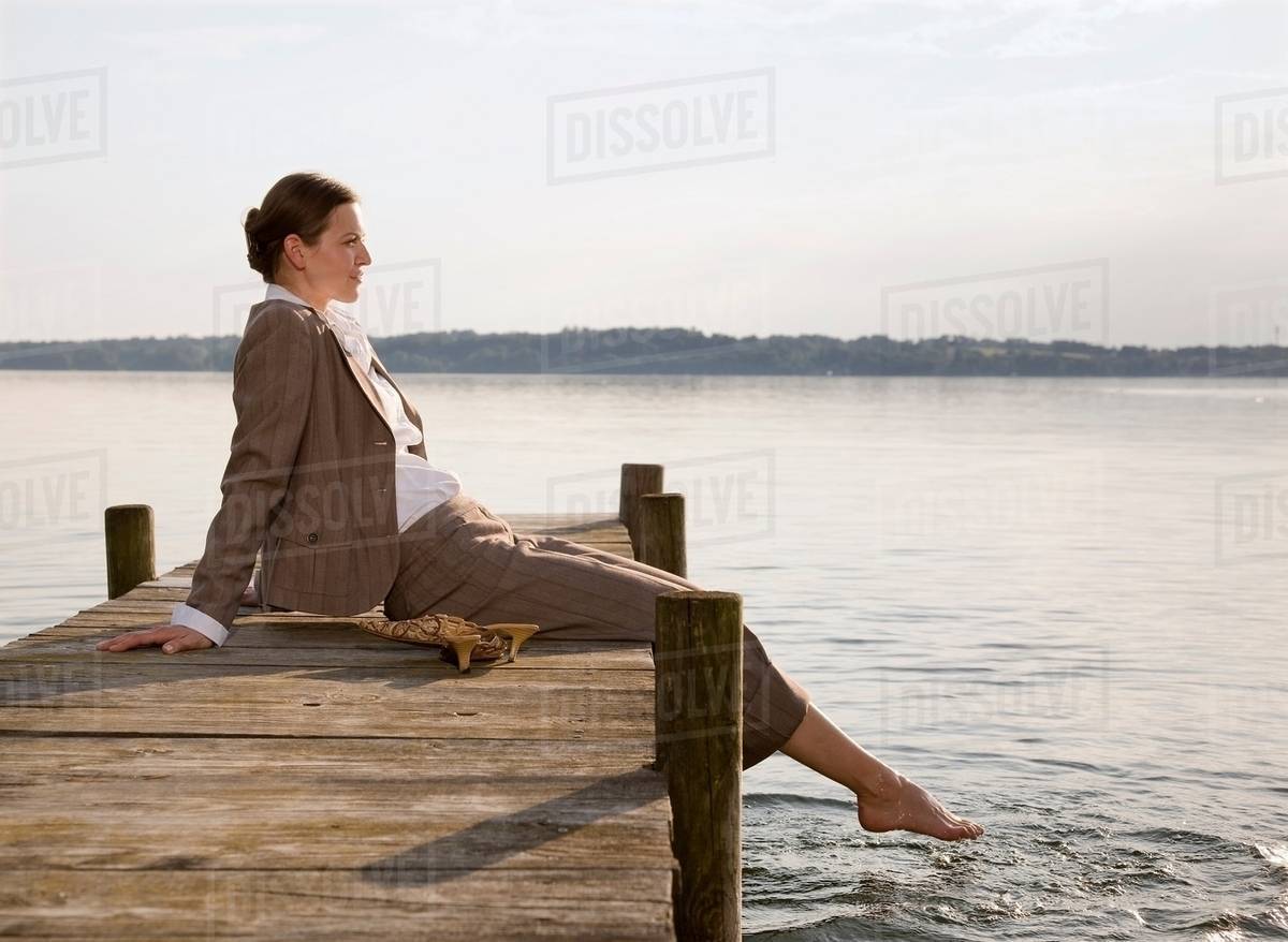 Woman sitting on pier at lake - Stock Photo - Dissolve
