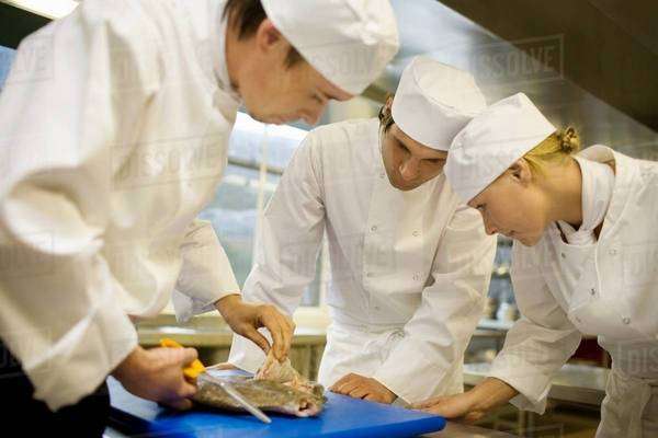 Three chefs filleting a fish - Royalty-free Stock Photo | Dissolve
