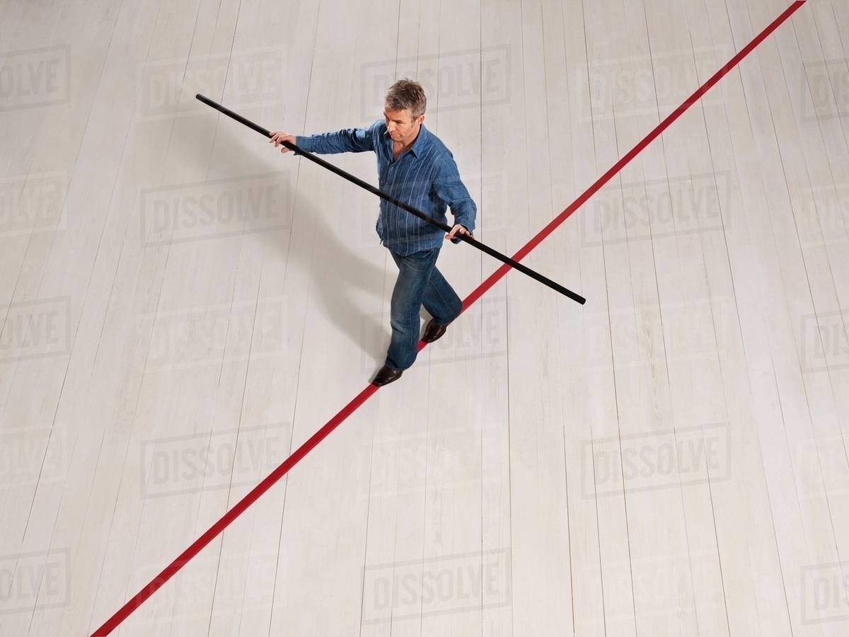 Man balancing on thin red line with pole - Stock Photo - Dissolve