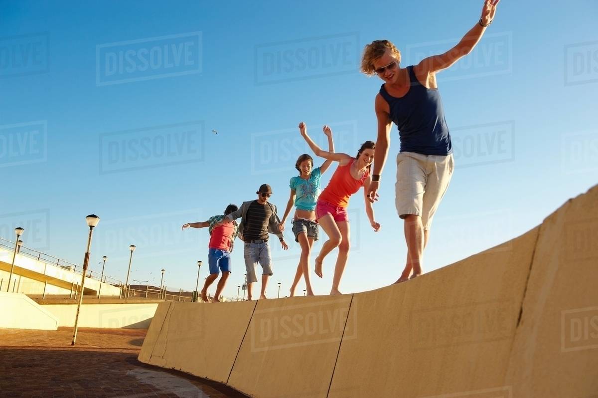 Young people balancing on wall - Stock Photo - Dissolve