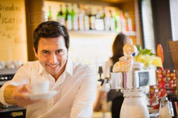Man serving coffee smiling in cafÃ© - Royalty-free Stock Photo | Dissolve