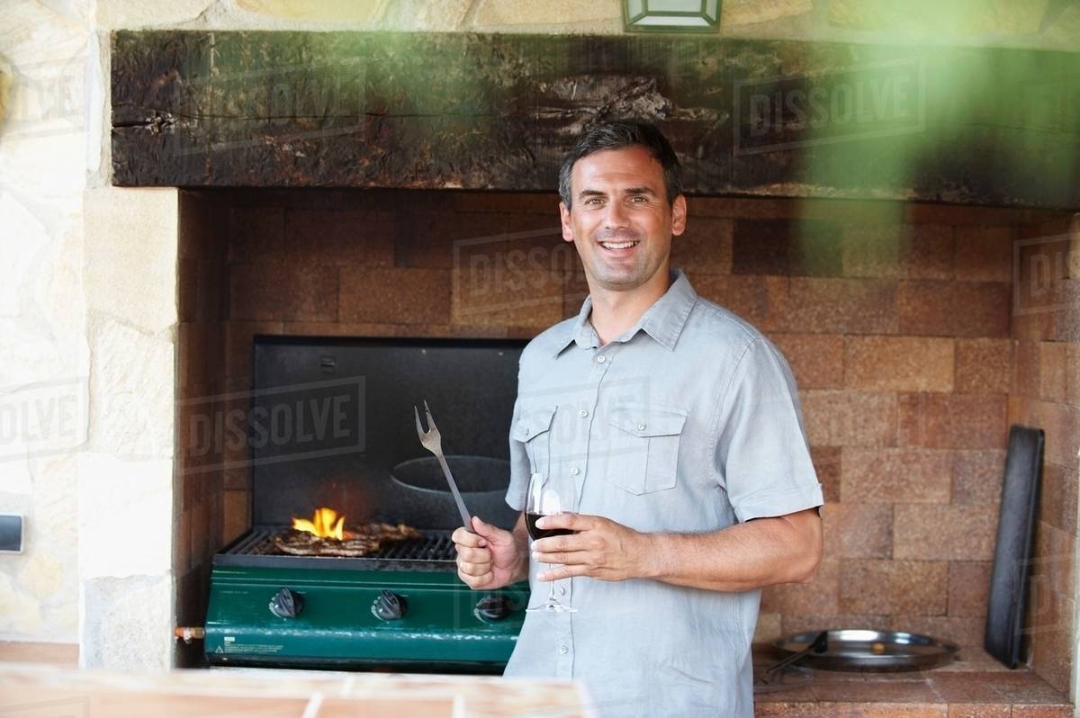 Smiling man standing by barbeque - Royalty-free Stock Photo | Dissolve